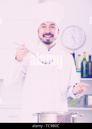 Smiling male cook checking taste of food while preparing in kitchen ...
