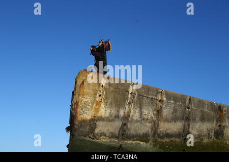 A lone piper plays on the Mulberry harbour at Arromanches in Normandy ...