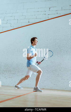 Full length view of squash player in red shorts holding racket and ...