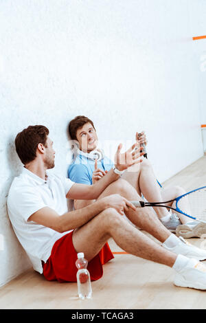 Two squash players talking while sitting on floor in four-walled court ...