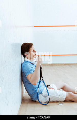 Tired squash player sitting on floor and opening bottle of water Stock ...