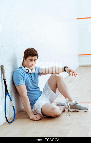 Squash player in blue polo shirt sitting on floor and looking at camera ...