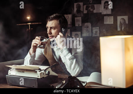 Detective talking on telephone and drinking cognac in office Stock ...