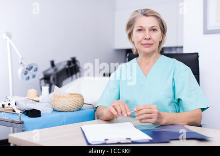 Mature female doctor cosmetologist working with documents in modern ...