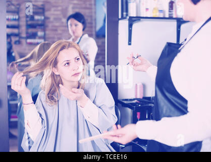 Upset blonde young female client blaming hairdresser as a haircut done ...