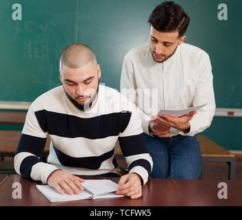 Portrait of two young guys working on their student project at desk in ...