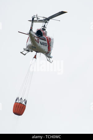 A Cal Fire helicopter flying around with water bucket in lake berryessa ...