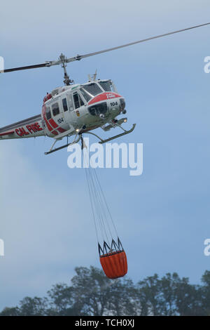 A Cal Fire helicopter flying around with water bucket in lake berryessa ...