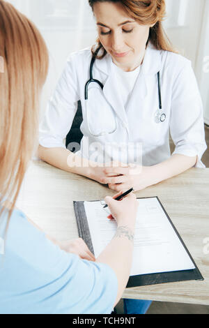 cropped view of donor signing registration form and doctor in white ...