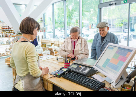 Elderly couple at cashier desk paying to teller in local zero waste ...