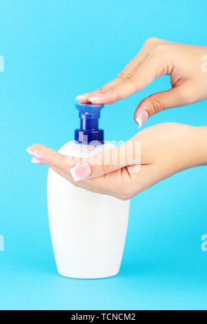 A woman squeezing a clear bottle of blue antibacterial gel on a wooden ...