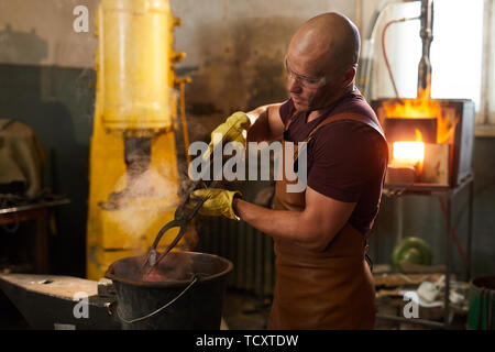 Blacksmith putting tongs in bucket of water at workshop Stock Photo - Alamy
