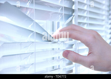 Someone looking out of window opening blinds Stock Photo - Alamy