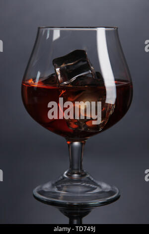 Brandy glass with ice on grey background Stock Photo - Alamy