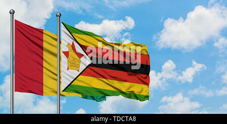 Zimbabwe and Guinea flag waving in the wind against white cloudy blue ...