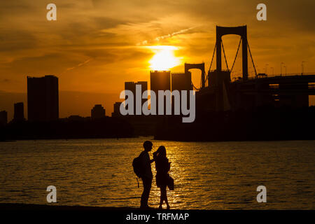 A young couple enjoys the view of Rainbow Bridge from a beach in Odaiba ...