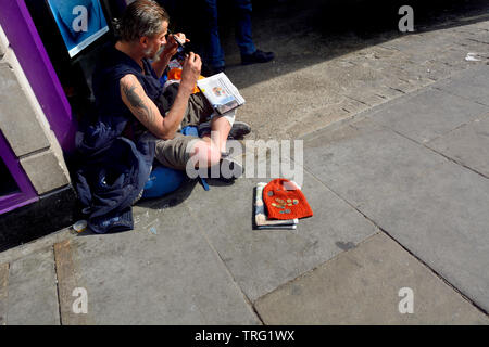 Rough sleeper / homeless person, reading a magazine next to an Evening ...