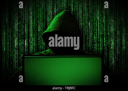 hacker with glowing mask behind notebook laptop in front of green source binary code background ...