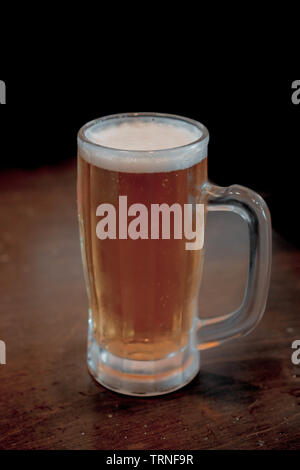 A glass mug filled with amber liquid sits on a wooden surface ...