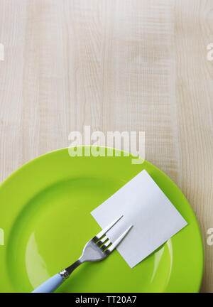 Empty note paper attached to fork, on plate, on color wooden background ...