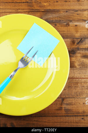 Empty note paper attached to fork, on plate, on color wooden background ...