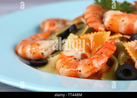 Fresh prawns with coloured macaroni and olives in a blue plate closeup ...