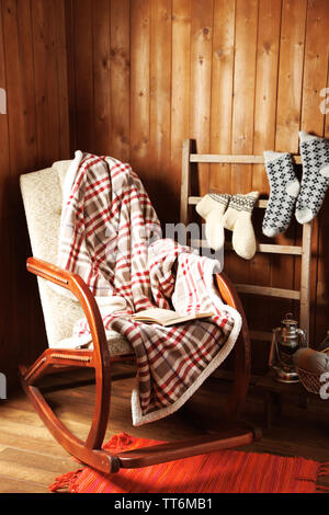 Rocking chair with plaid and book near wooden wall Stock Photo - Alamy