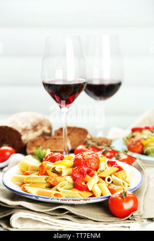 Pasta salad with vegetables and two glasses of red wine on wooden table ...