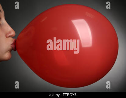 Young woman inflating a huge red balloon by mouth Stock Photo - Alamy