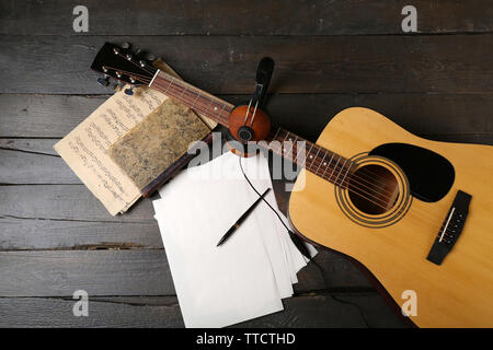 Acoustic guitar, headphones, musical notes and white papers on wooden ...