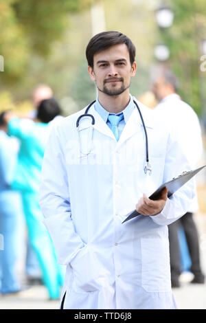 Smiling doctor with clipboard and staff behind her Stock Photo - Alamy