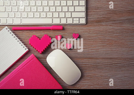 Computer peripherals with pink hearts, pen and notebooks on wooden ...