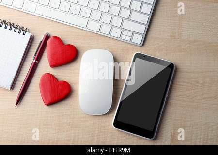 Computer peripherals with hearts, notebook and mobile phone on wooden ...