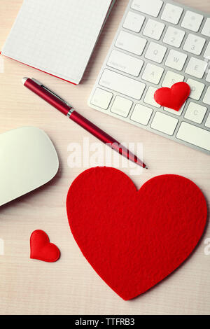 Computer peripherals with red hearts, pen and notebook on light wooden ...