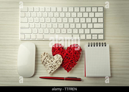 Computer peripherals with wicker hearts, pen and notebook on light ...