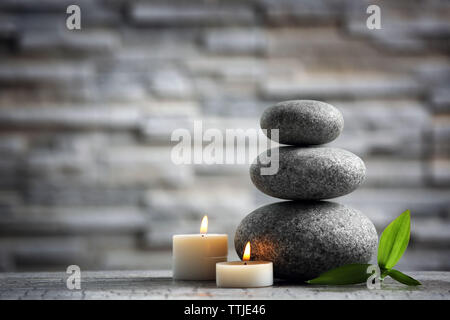 Composition of spa pebbles, candles and bamboo leaf on grey background ...