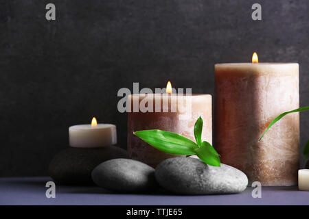 Composition of spa pebbles, candles and bamboo leaf on grey background ...