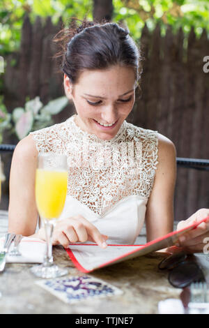 Woman holding menu, reading it while sitting at restaurant table with ...