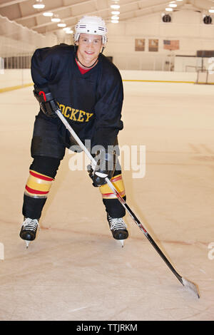Portrait of young hockey player with stick standing on one knee on ice ...