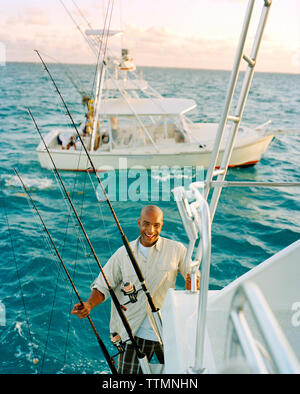 Smiling mid adult man fishing while standing on the deck of a boat with ...