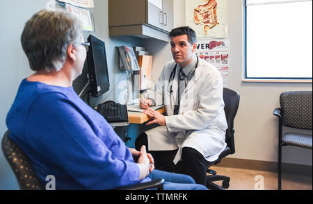 Doctor taking patient history from older woman at a desk in a clinic ...