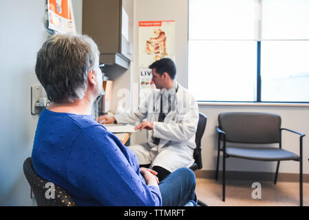 Doctor taking patient history from older woman at a desk in a clinic ...