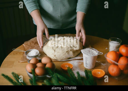 Midsection of woman kneading dough on wooden table in kitchen at home ...