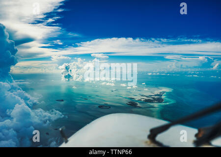 Cropped image of airplane flying against blue sky over scenic view of ...