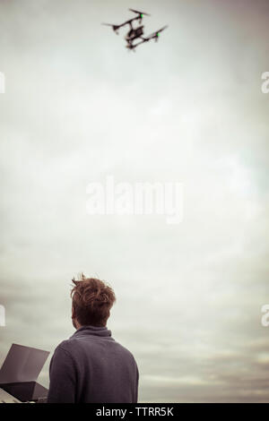 Low angle view of man with camera looking up while standing in forest ...