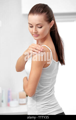 Woman applying body cream onto her arm against beige background ...