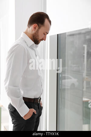 Depressed handsome man standing near window Stock Photo - Alamy