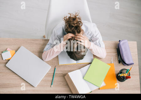 girl doing homework on a wooden table and there was a pile of books ...