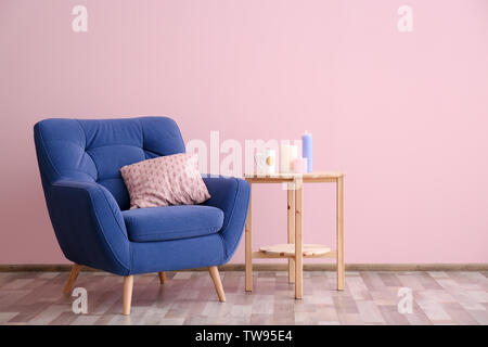 Soft armchair and side table near color wall Stock Photo - Alamy