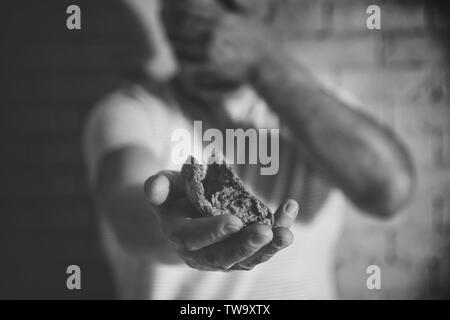 Poor man with little piece of bread on brick wall background. Black and ...